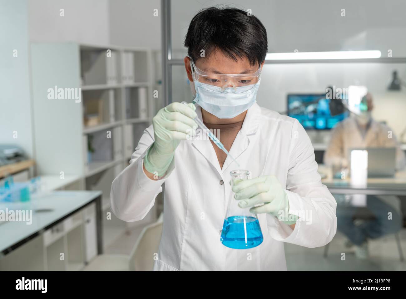 Young Asian female chemist adding drop of chemical substance into blue ...