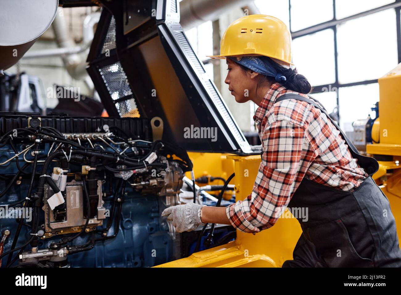 Young female technician in coveralls and hardhat checking motor of ...