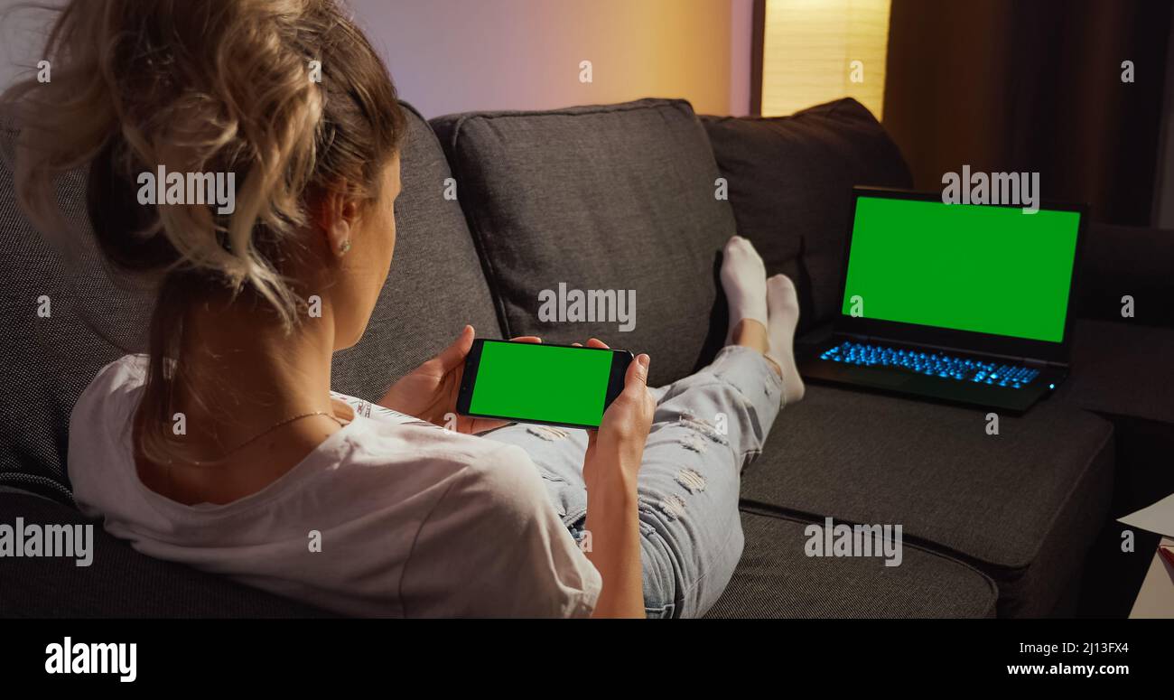 Over the shoulder view woman lying on a sofa using phone and laptop ...