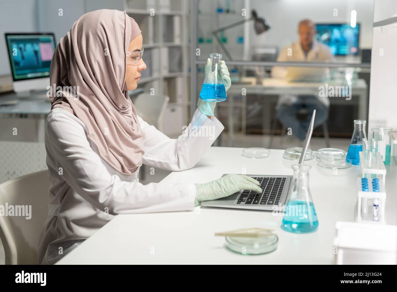 Side view of young Muslim female scientist in hijab looking at test ...