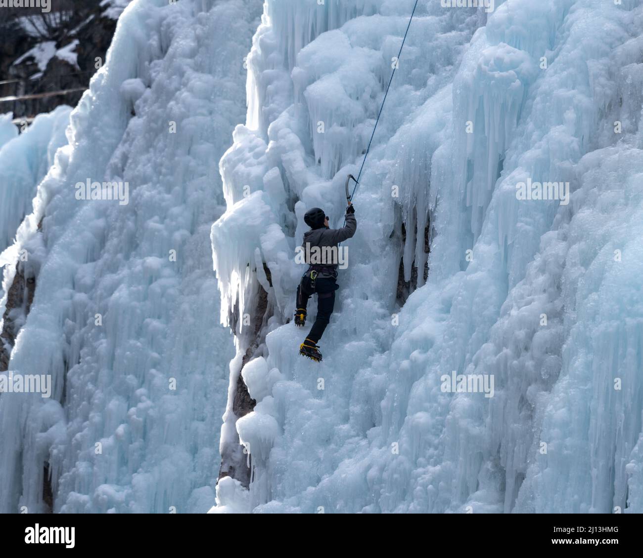 A female ice climber ascends an ice wall 160' high using ice axes and ...
