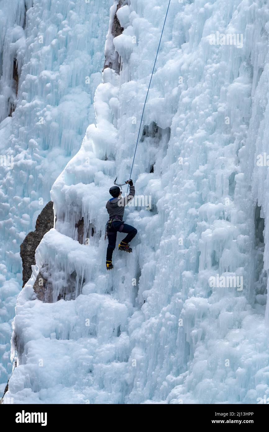 A female ice climber ascends an ice wall 160' high using ice axes and ...