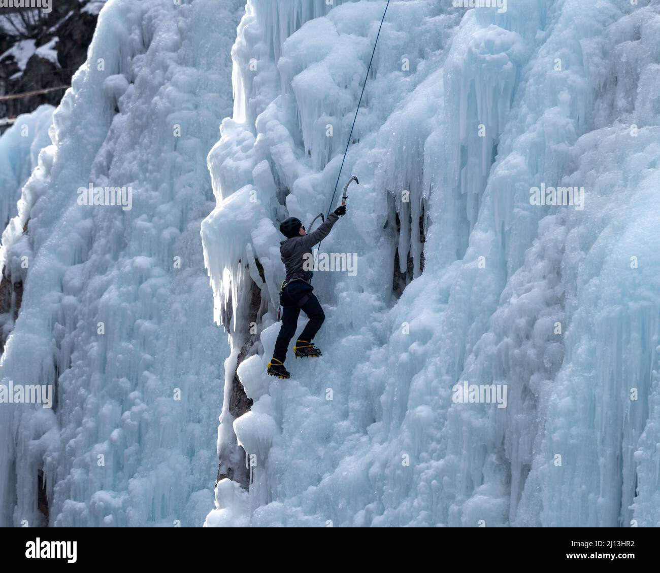 A female ice climber ascends an ice wall 160' high using ice axes and ...