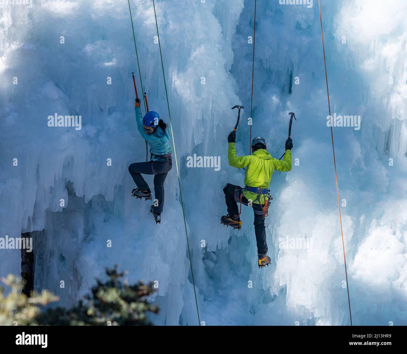 Male and female ice climbers ascending an ice wall using ice axes and ...