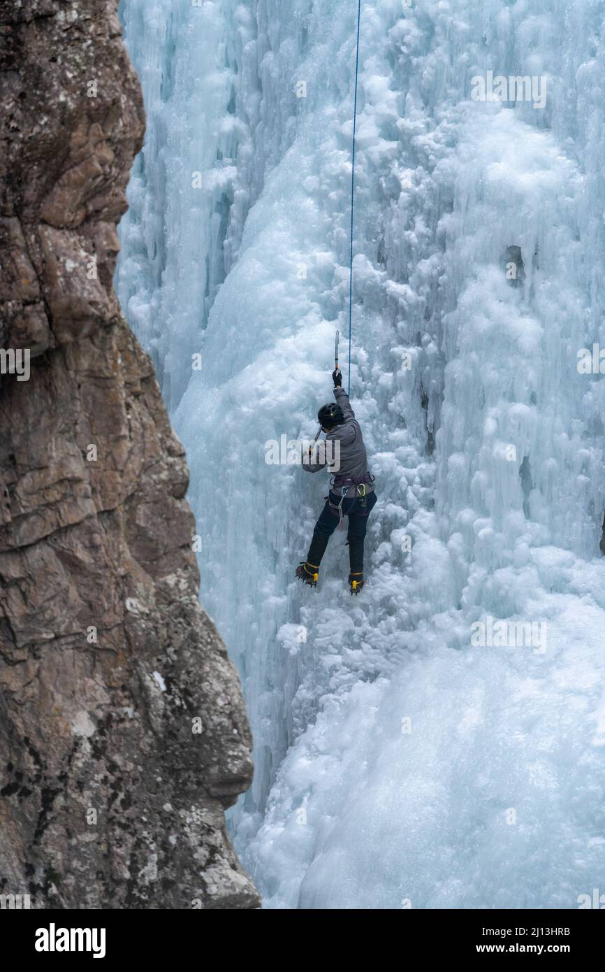 A female ice climber ascends an ice wall 160' high using ice axes and ...
