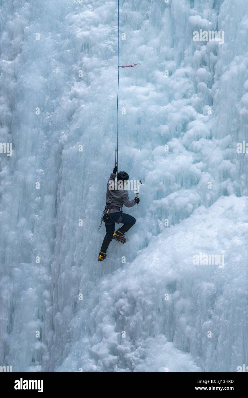 A female ice climber ascends an ice wall 160' high using ice axes and ...