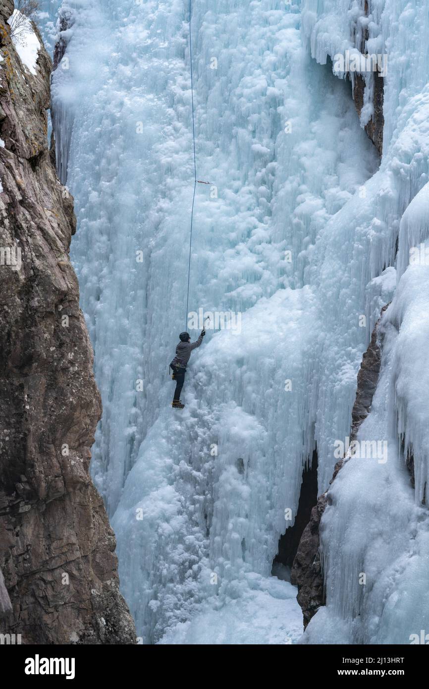 A female ice climber ascends an ice wall 160' high using ice axes and ...