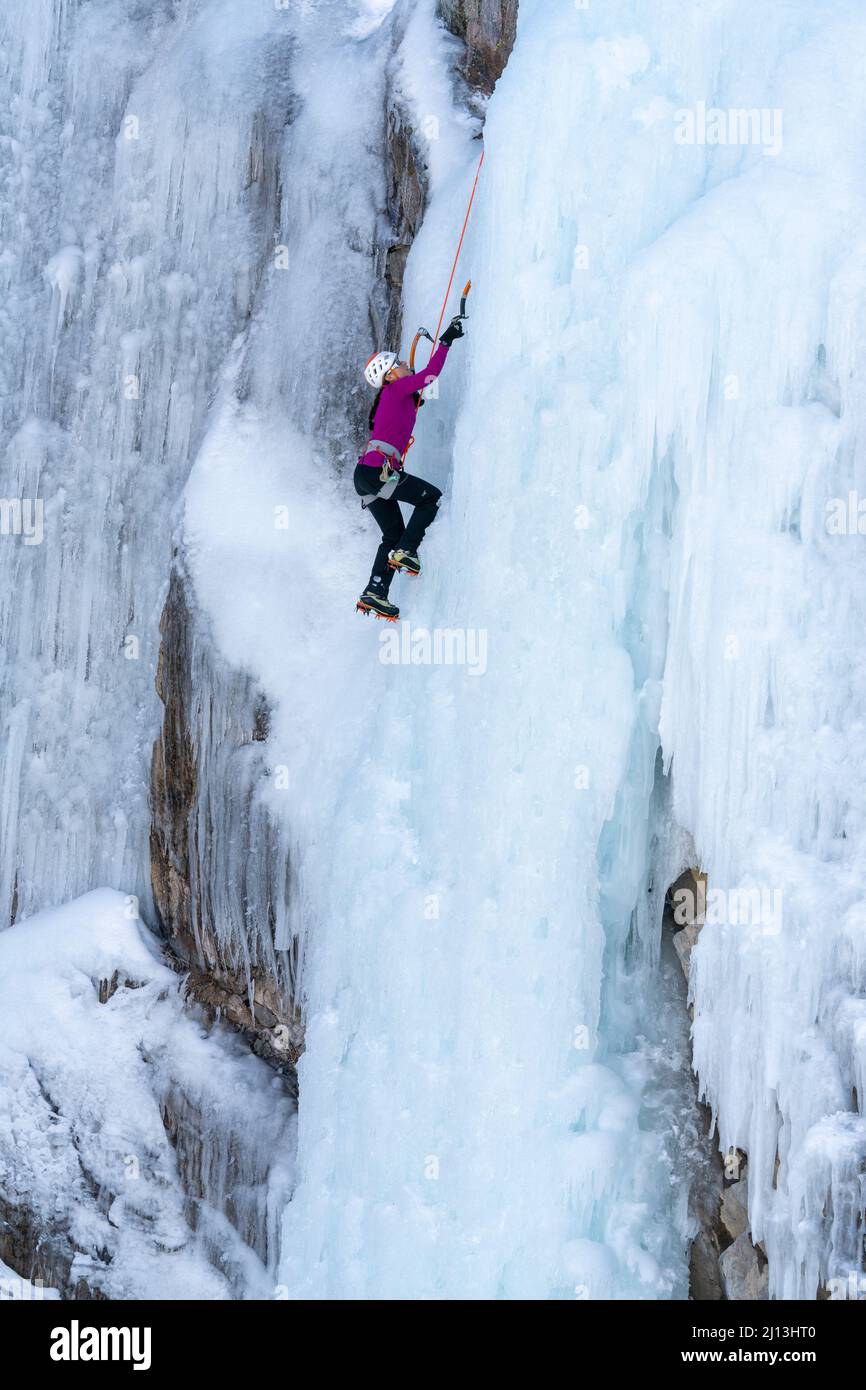 A female ice climber ascending an ice wall using ice axes and crampons ...