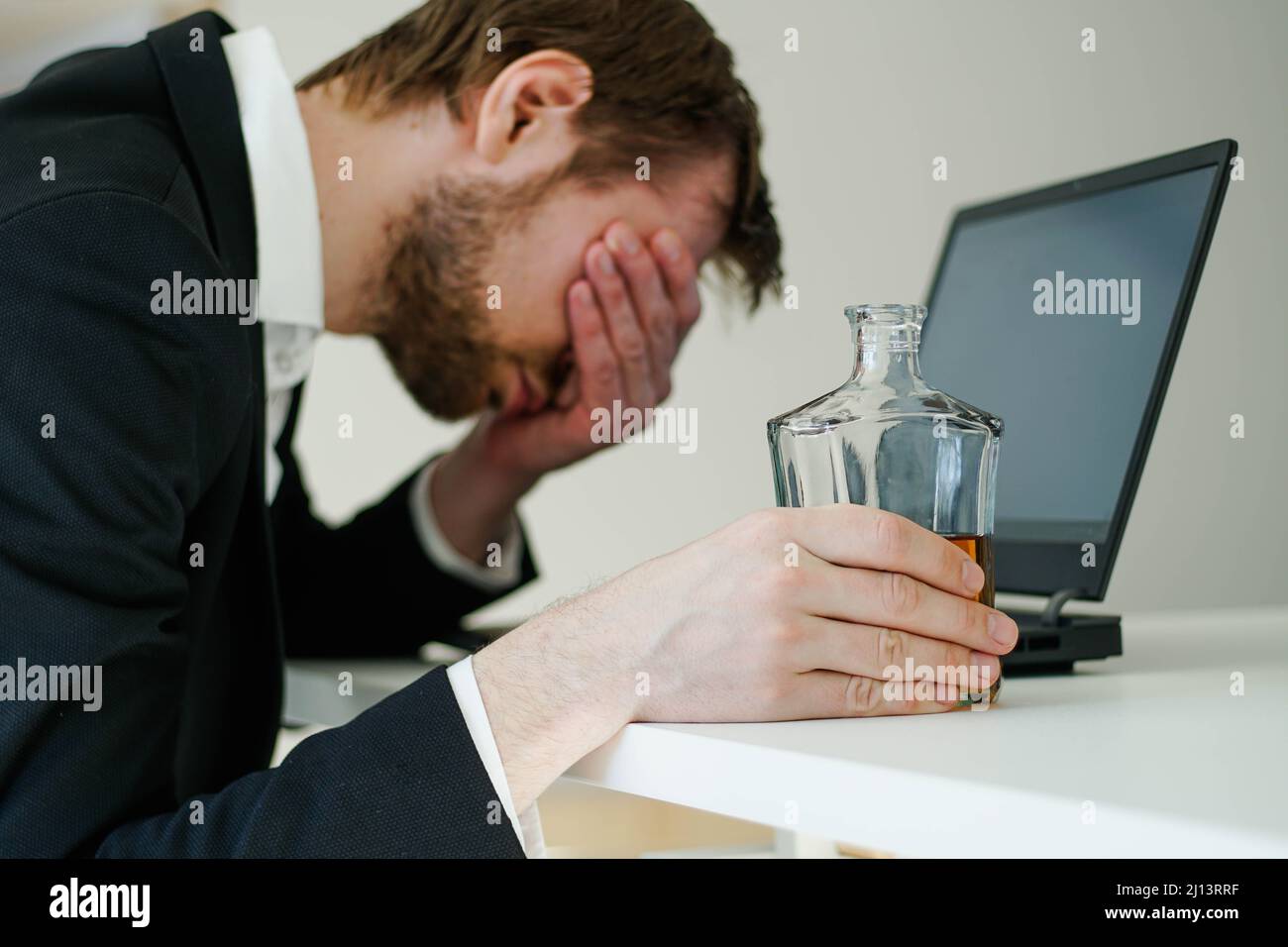 Fatigue young businessman sitting at workplace and holding whiskey ...