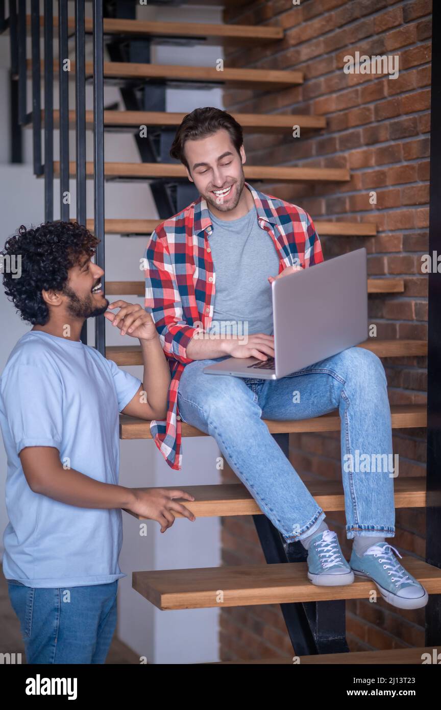 Joyous man watching his boyfriend working on the computer Stock Photo ...