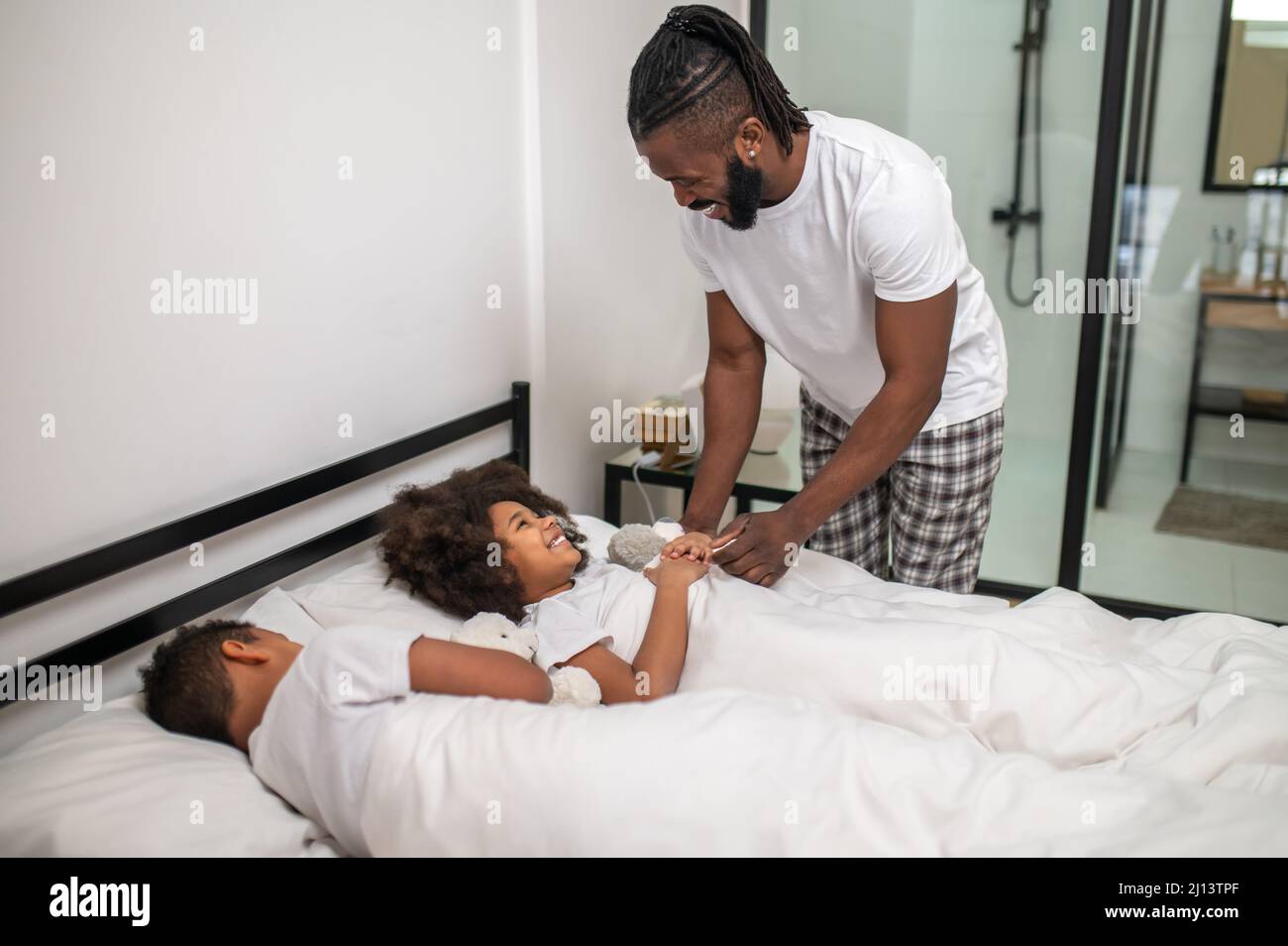 Man leaning over children in bed Stock Photo - Alamy