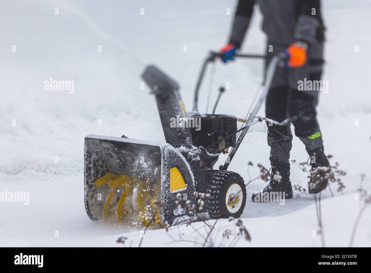 Process of removing snow with portable blower machine, worker dressed in overall workwear with ...
