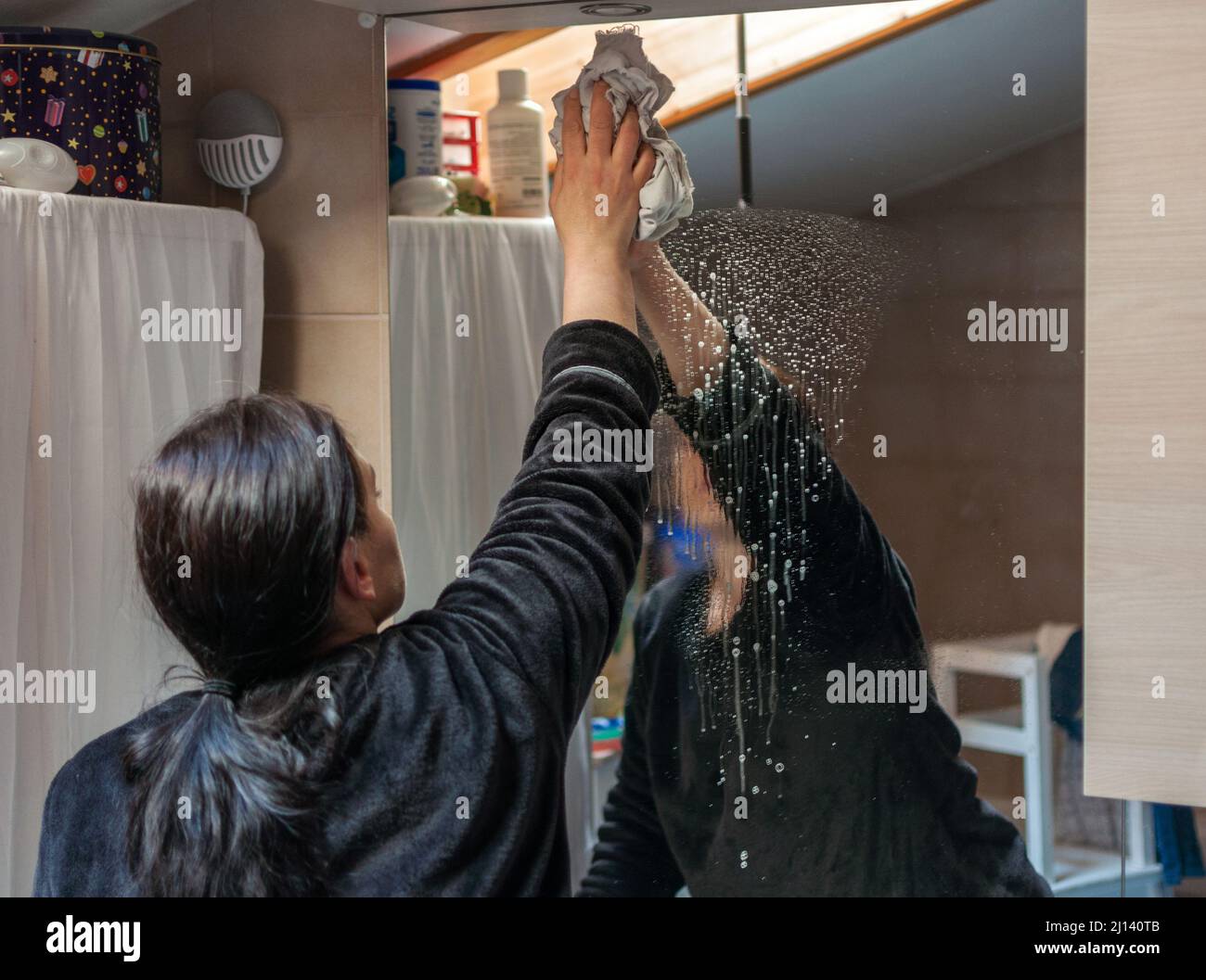 housewife wipes a mirror with a cloth. seen from behind and partially ...