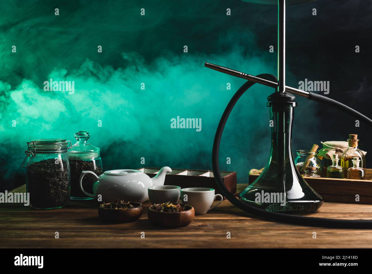 Hookah, dry tea and teapot on wooden surface on black background with ...