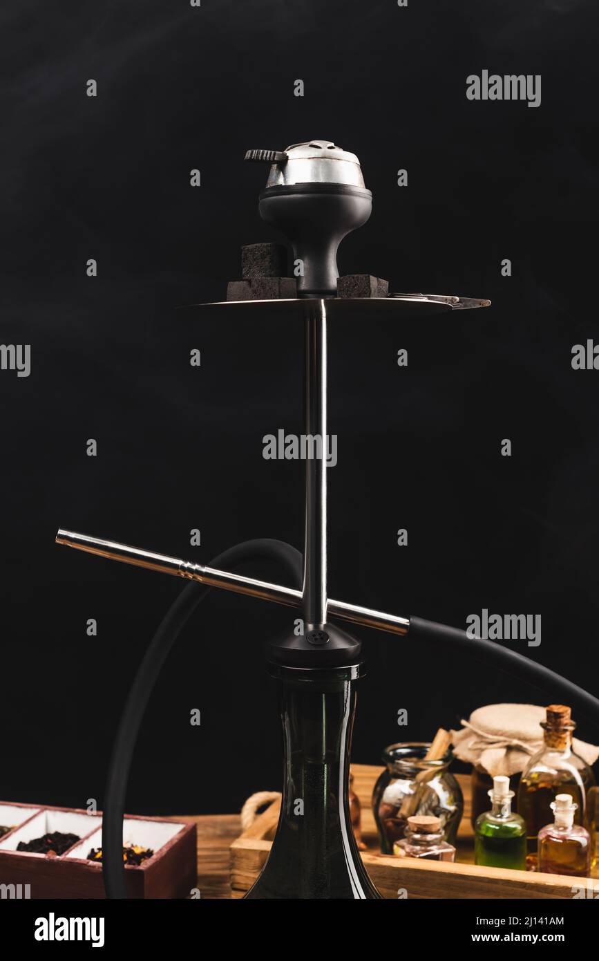 Hookah with coals near blurred dry tea on black background with smoke ...