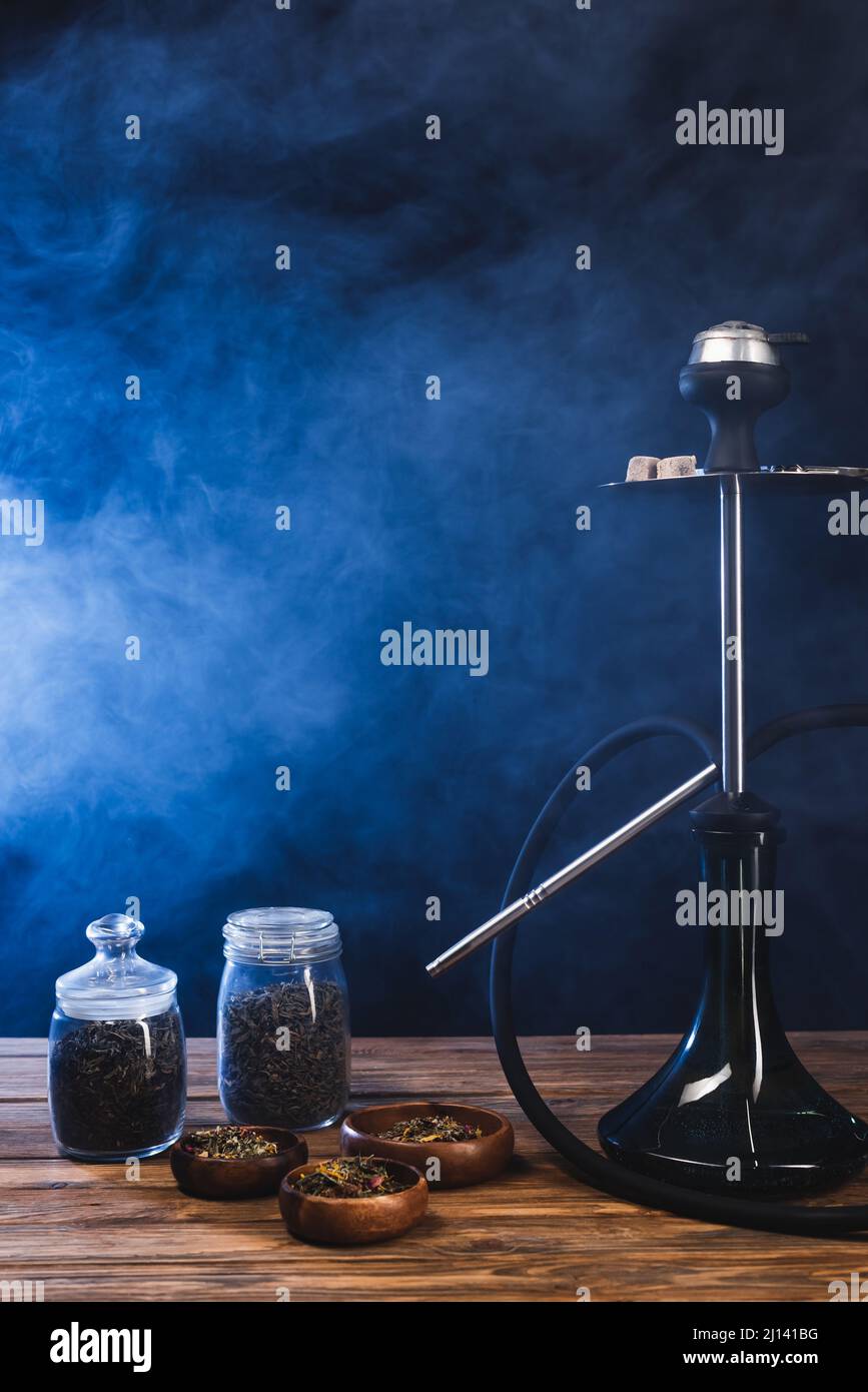 Hookah near dry tea in bowls on wooden surface on black background with ...
