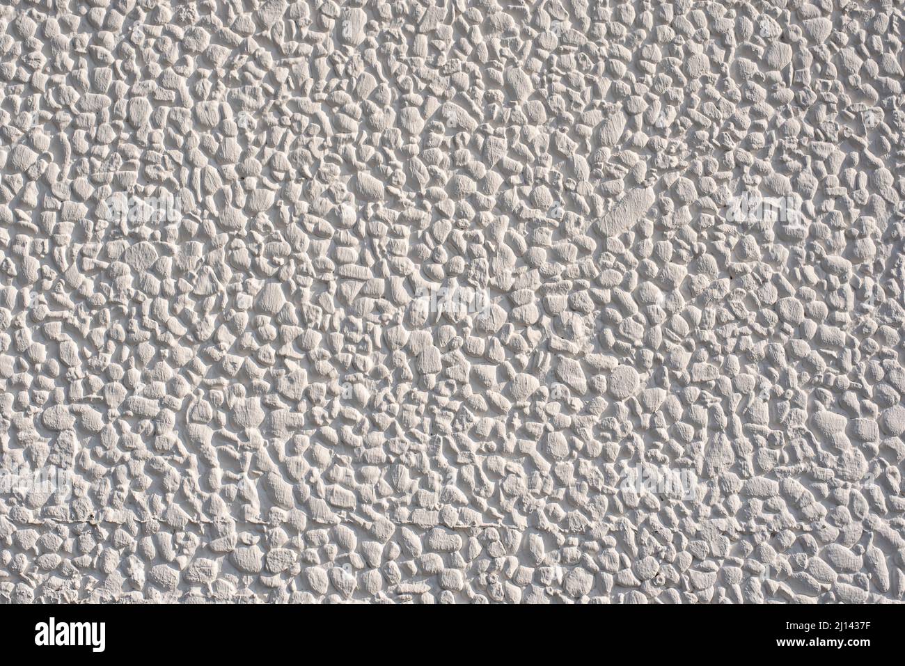 a wall covered with small pebbles and painted white in bright sunshine ...