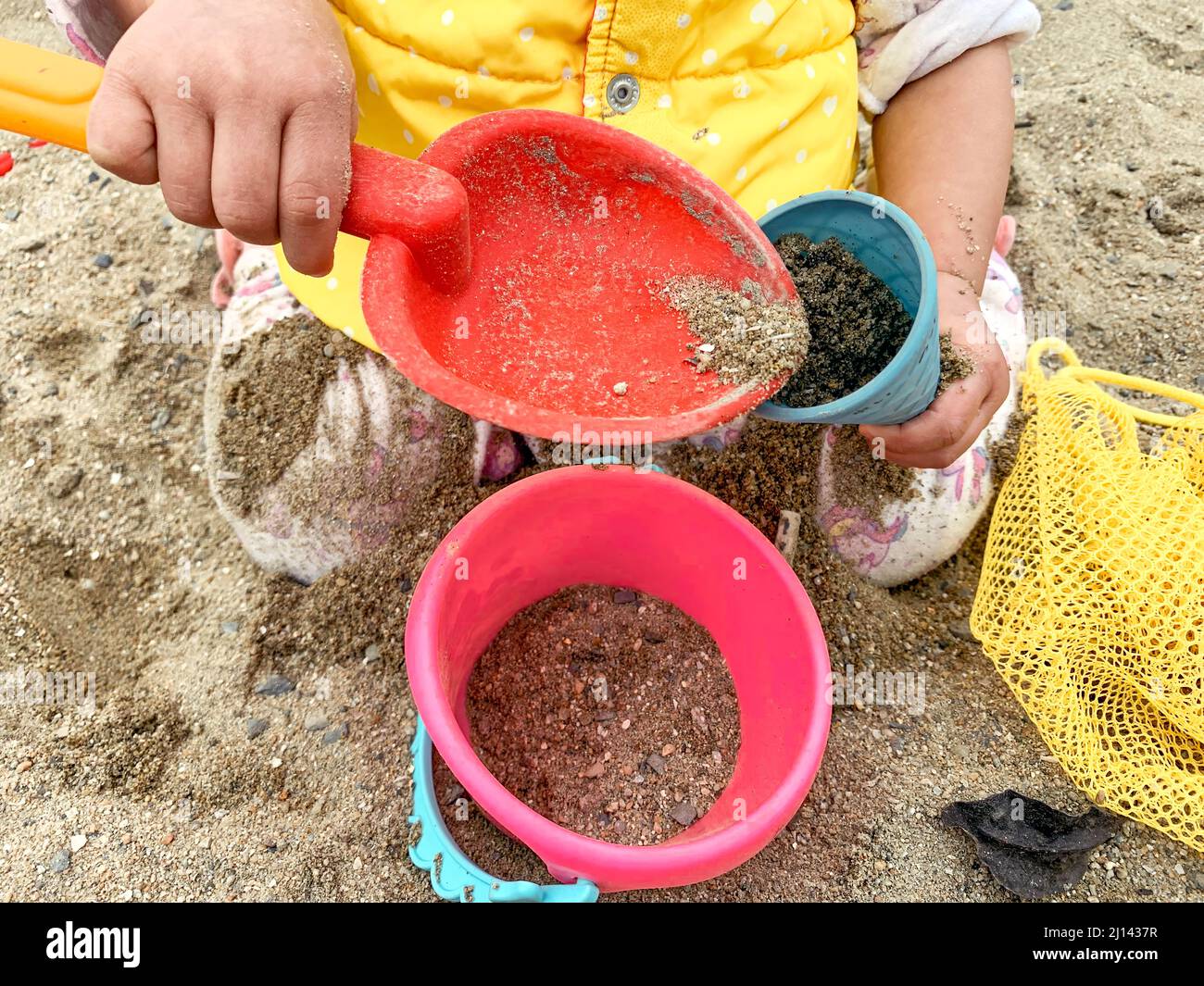 Child playing in the sandpit with a shovel and scooping the sand into a ...