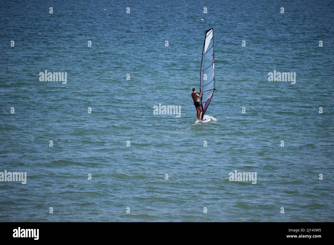 The man is engaged in windsurfing against the background of blue sea ...