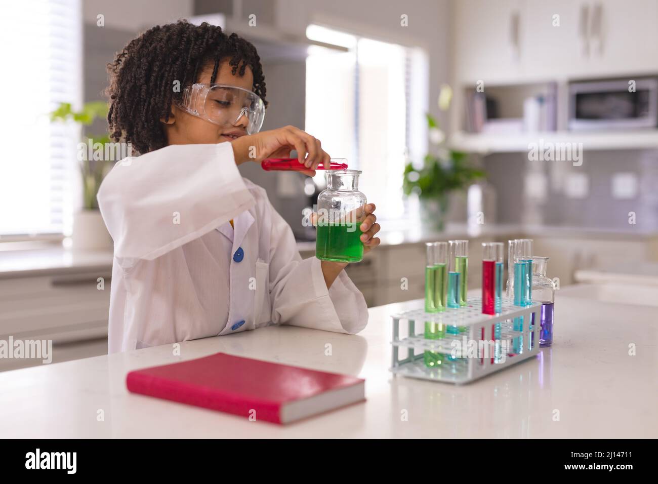Hispanic boy wearing lab coat and eyewear pouring chemical solution in ...