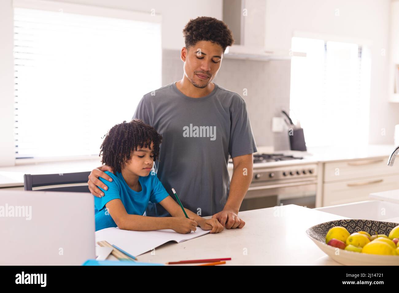Hispanic man standing by son doing homework at dining table in kitchen ...