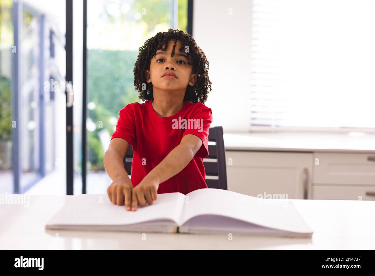 Cute hispanic boy reading book with braille while sitting in kitchen at ...