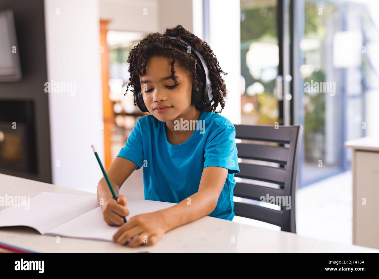 Hispanic boy wearing headphones writing in book while studying at home ...