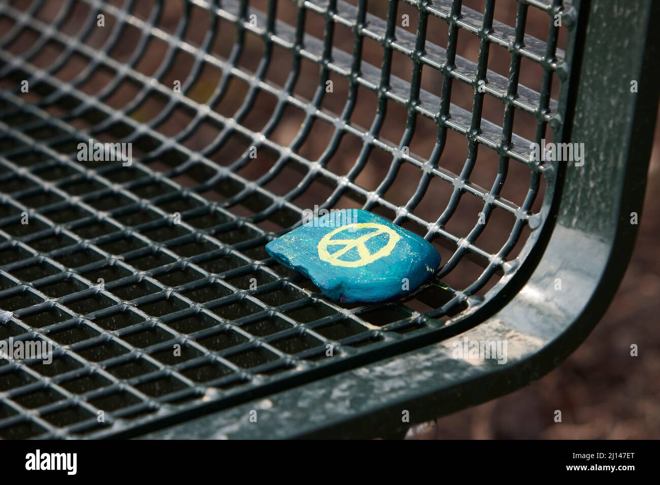 blue painted stone with yellow peace sign laying on a green metal park ...