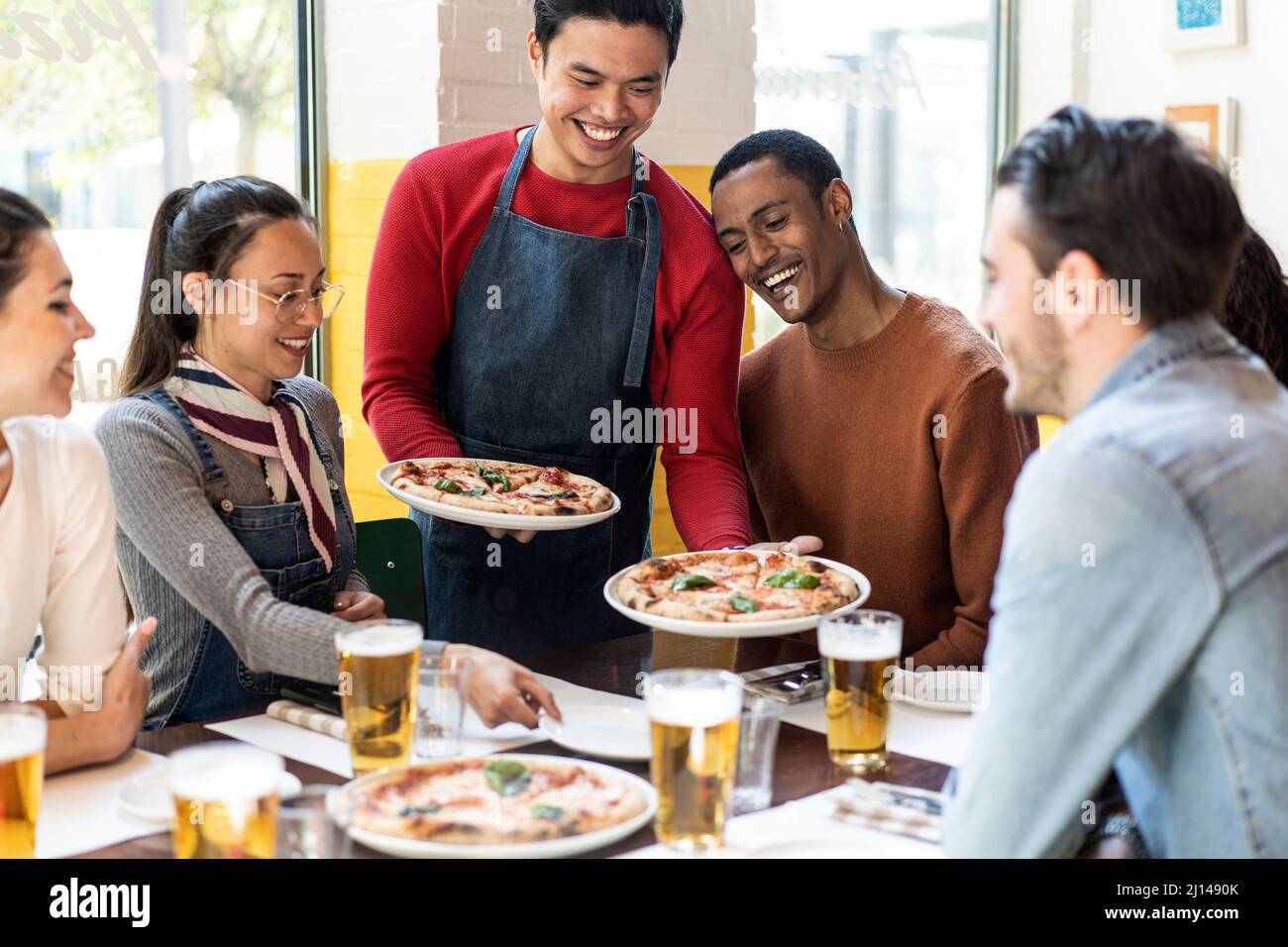Confidant waiter serving delicious pizzas margherita to multicultural ...