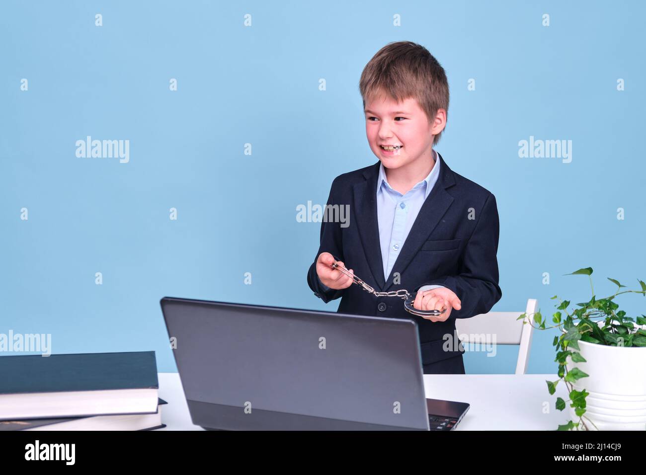 A boy in a school suit with handcuffs on his hands at a table with a ...