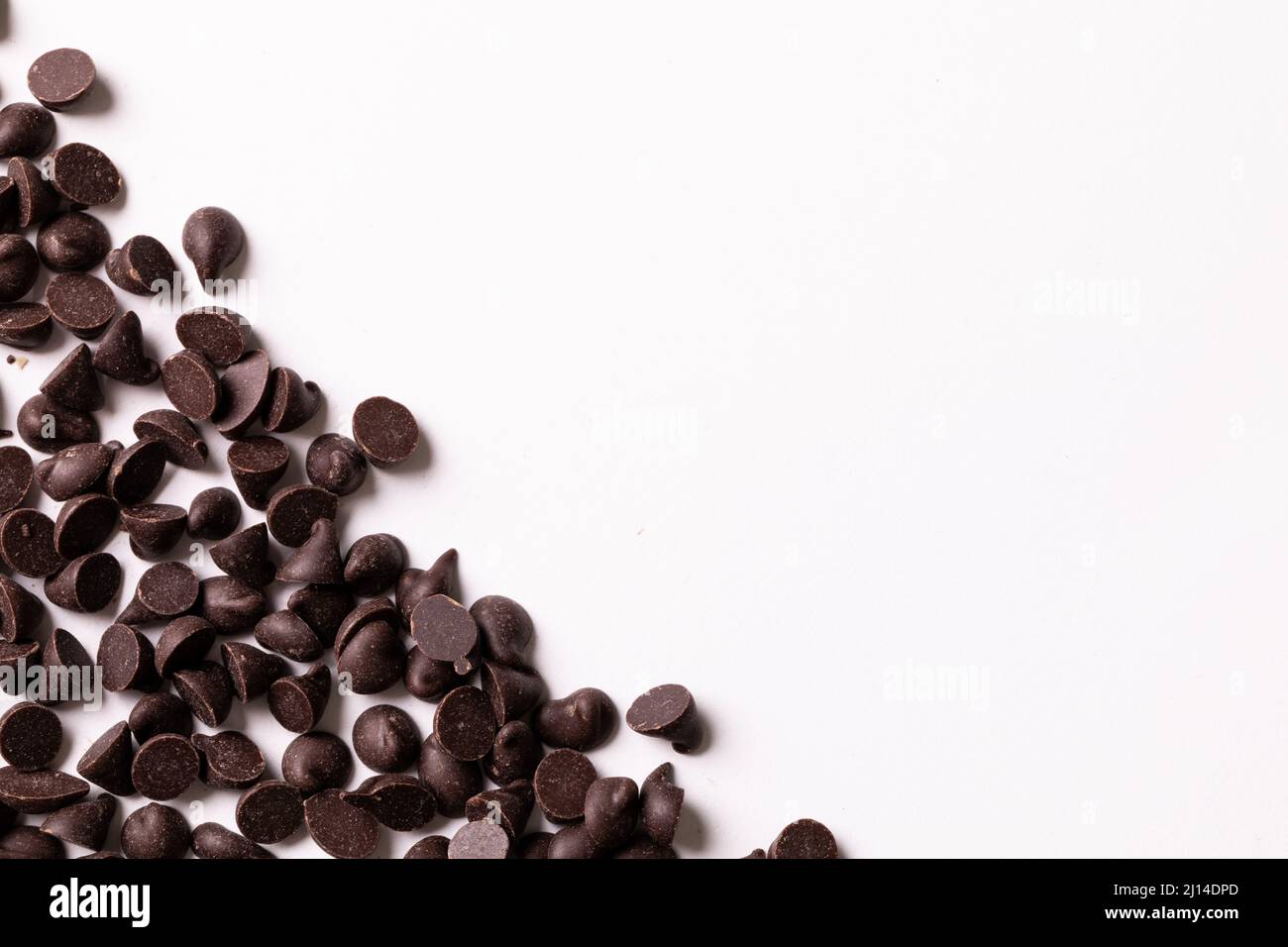 Overhead view of fresh chocolate chips scattered by copy space on white ...