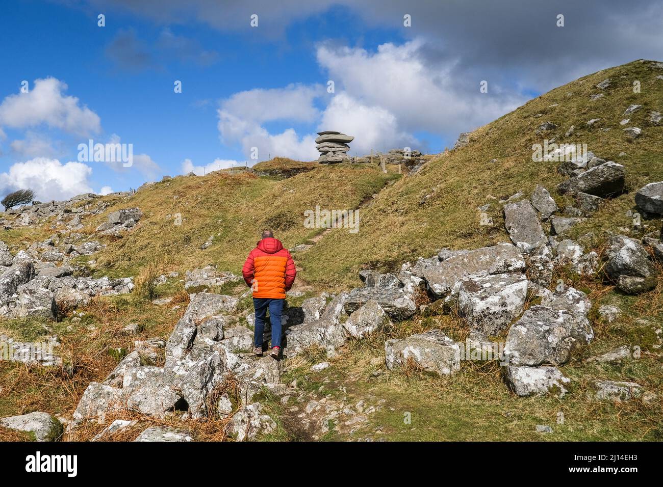 A walker in a bright red jacket walking up a rough footpath to the ...