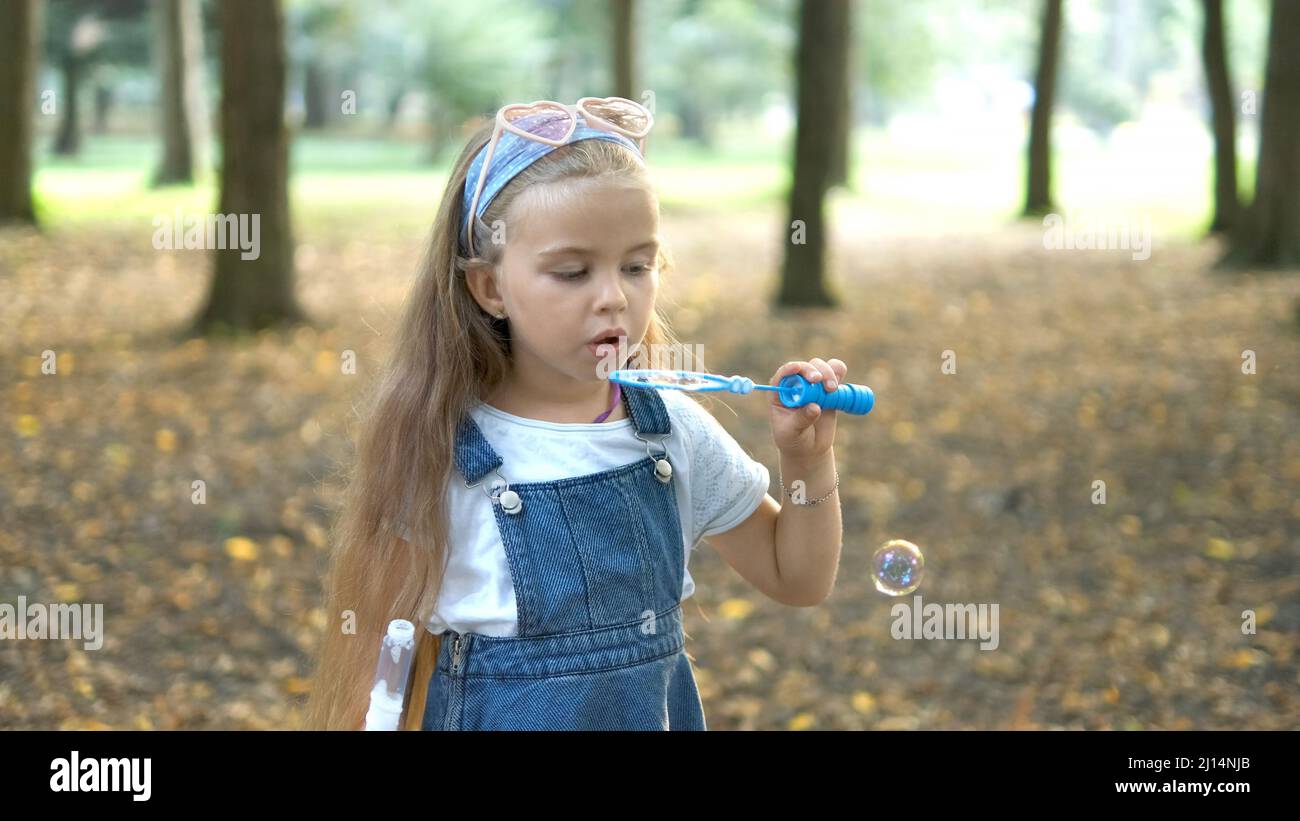 Little happy child girl blowing soap bubbles outside in green park ...