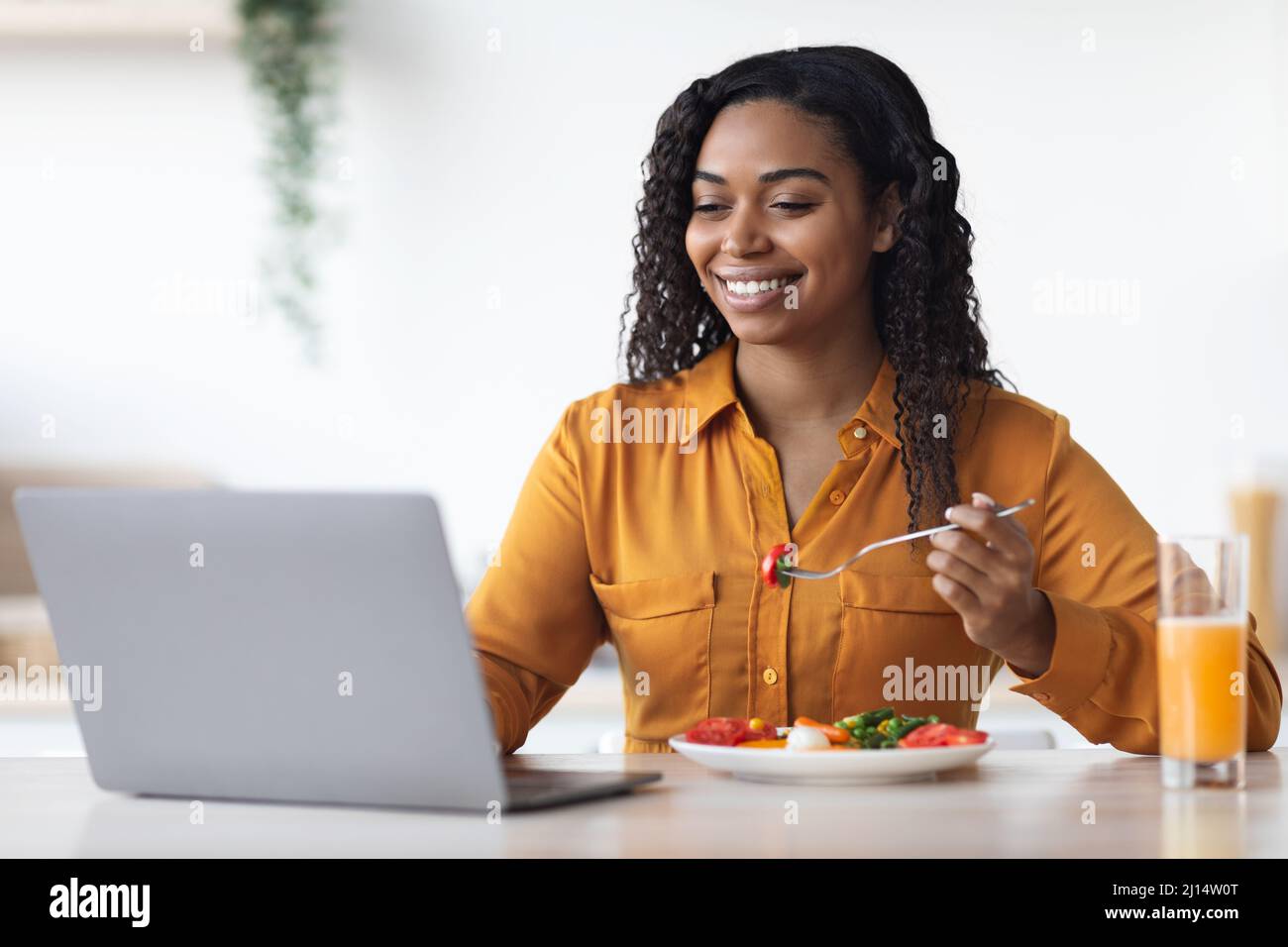 Cheerful african american woman having snack in front of laptop Stock ...