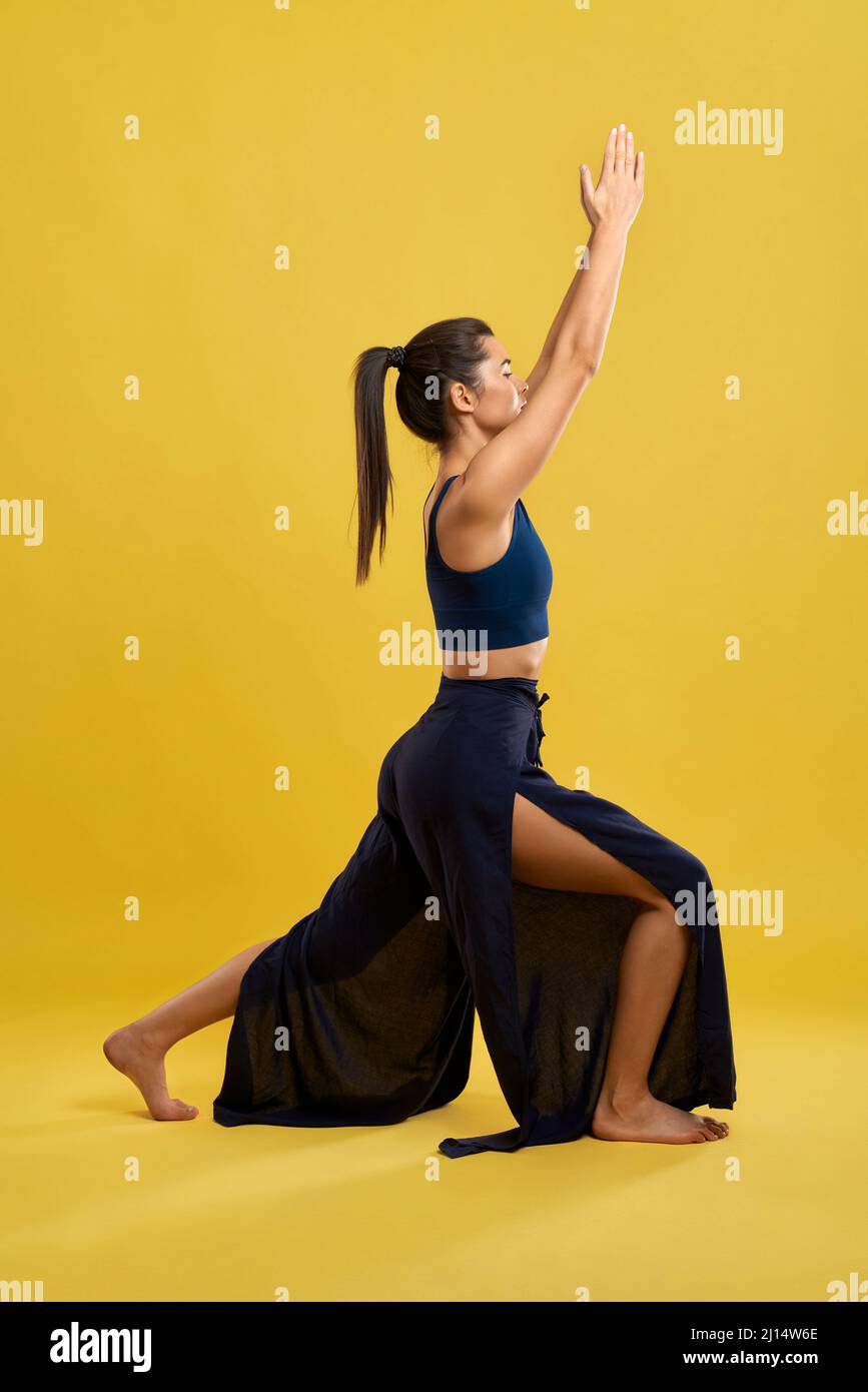 Side view of sporty female standing with bent legs, raising hands ...