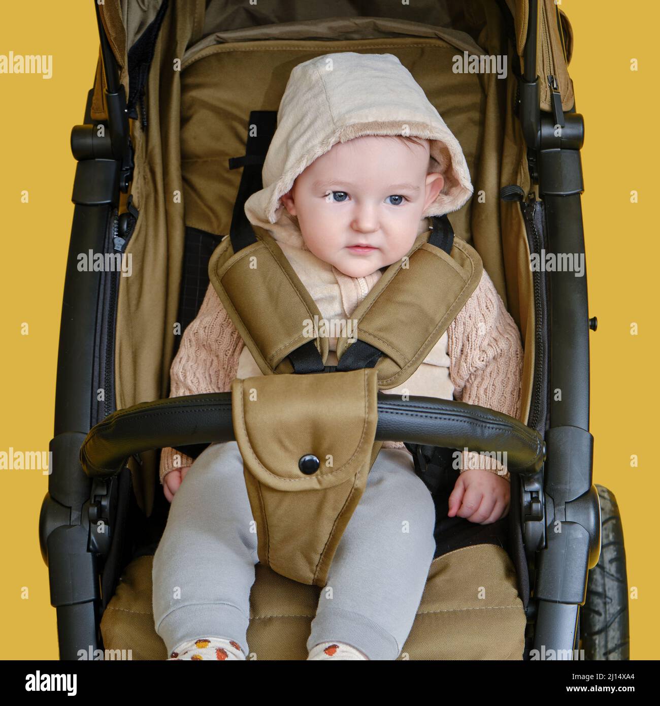 A happy child is sitting in a baby carriage on a studio yellow ...