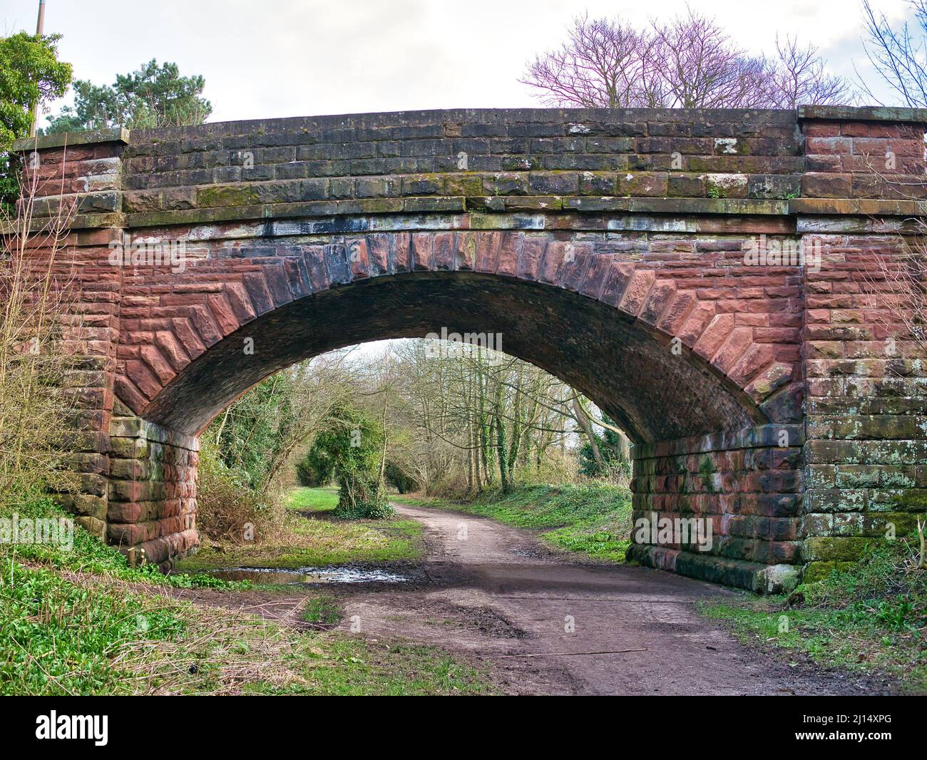 An old, arched, sandstone bridge over a disused railway line, now the ...