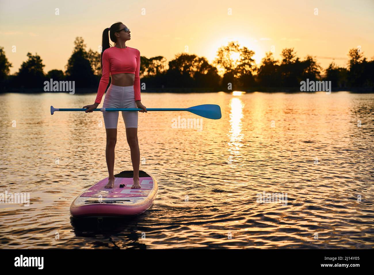 Attractive woman with slender body floating on sup board during evening ...