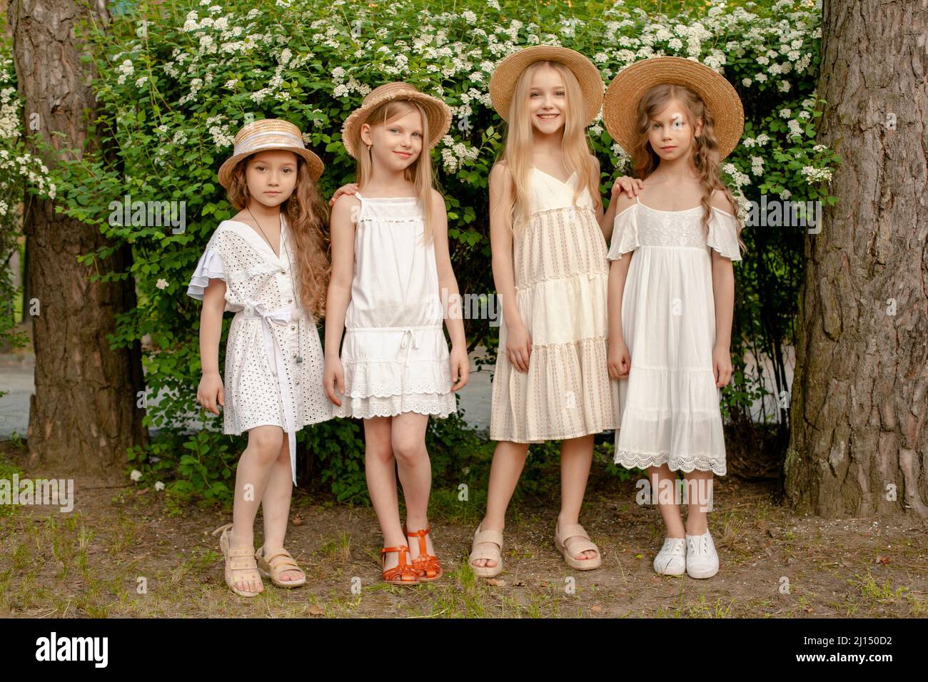 Cute preteen girls in light dresses standing near flowering bush in ...