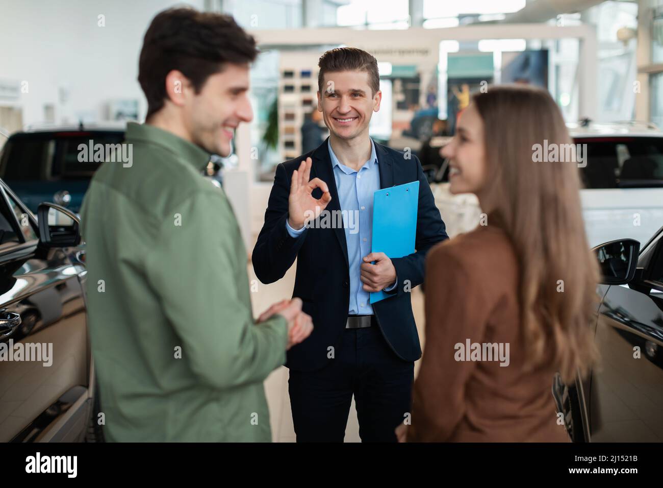 Auto showroom manager showing okay gesture to happy young customers at ...