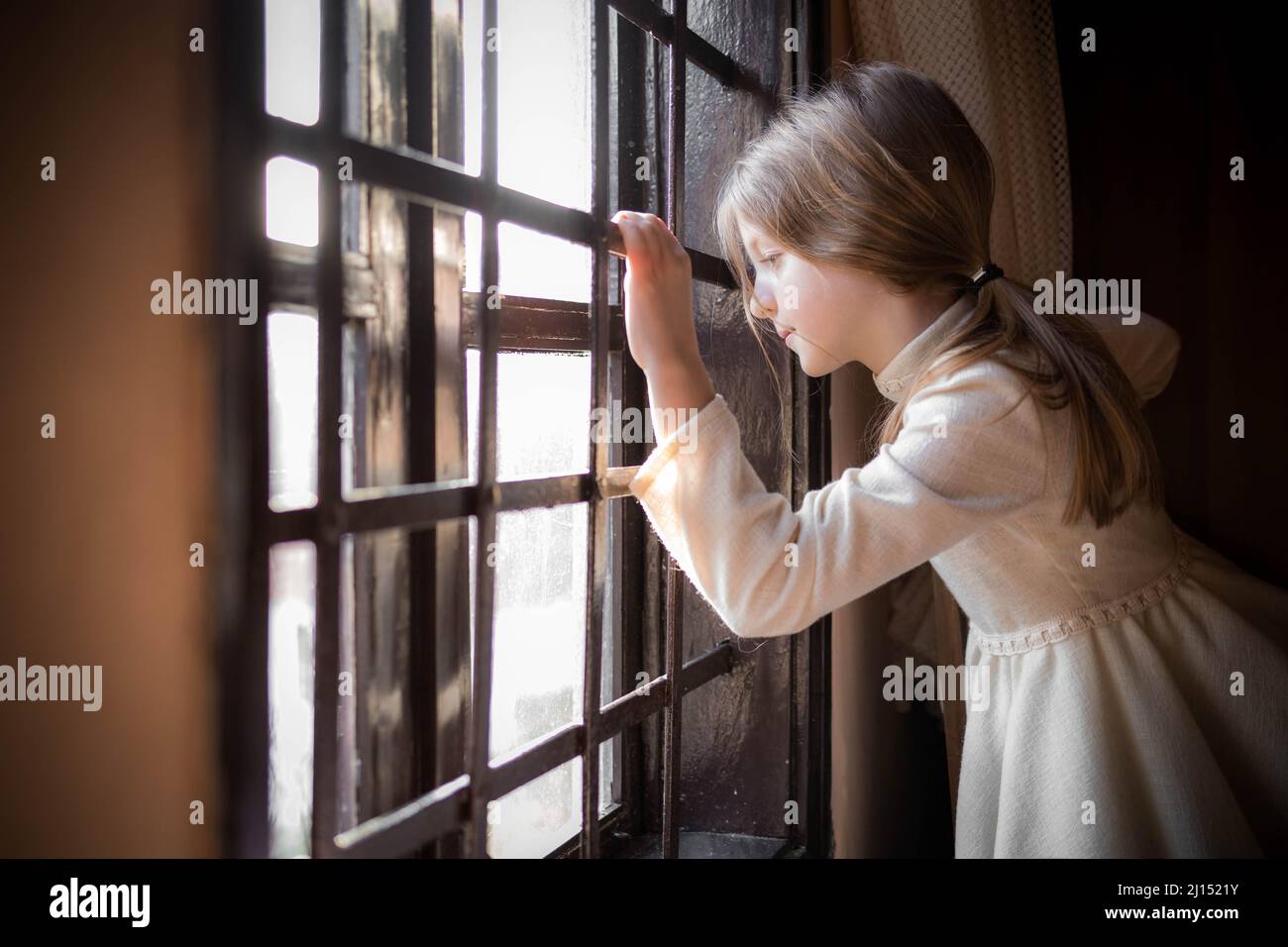 Little blonde girl looking through the window, longingly Stock Photo ...