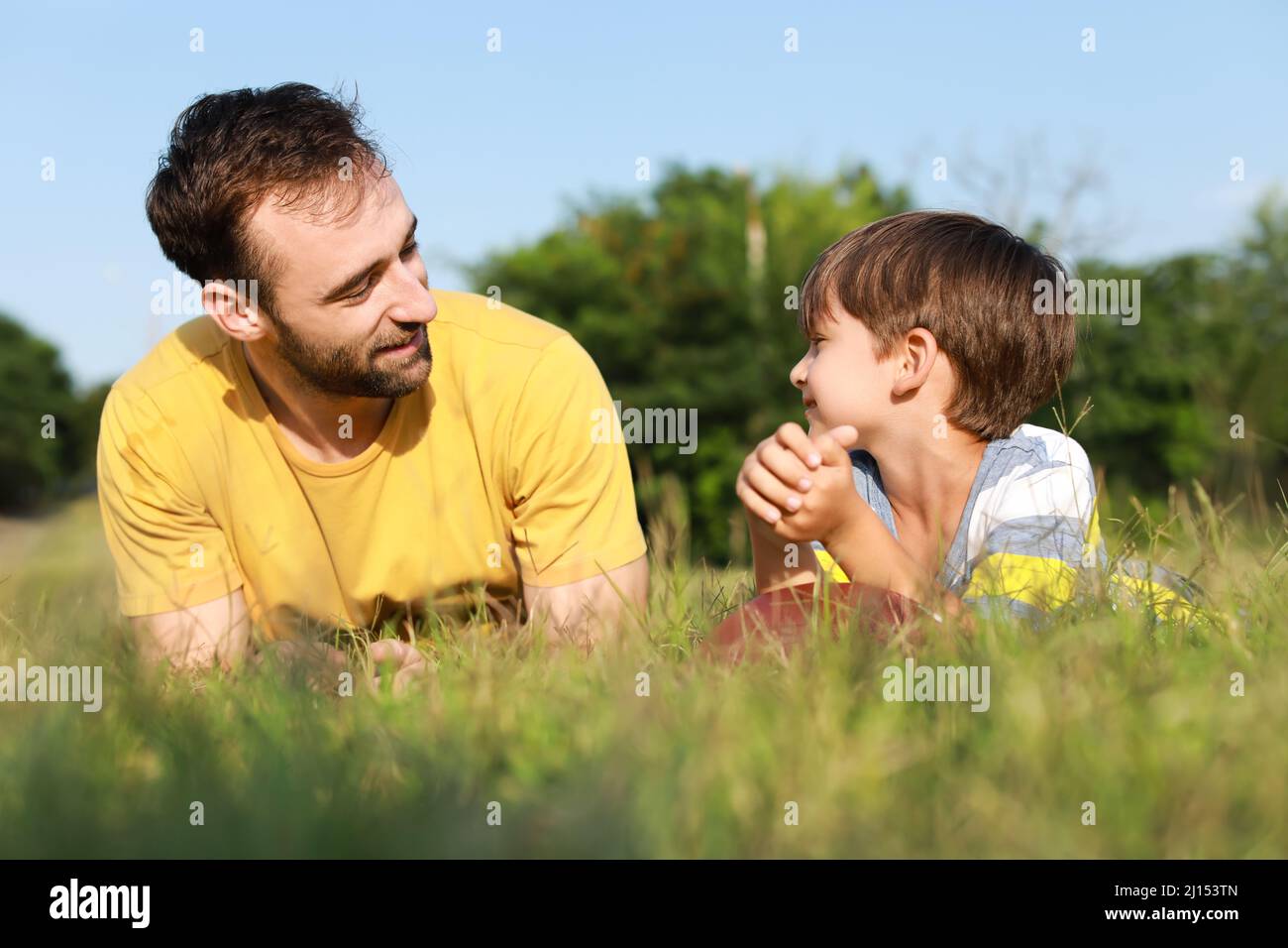 Little boy with rugby ball and his father lying on green grass in park ...