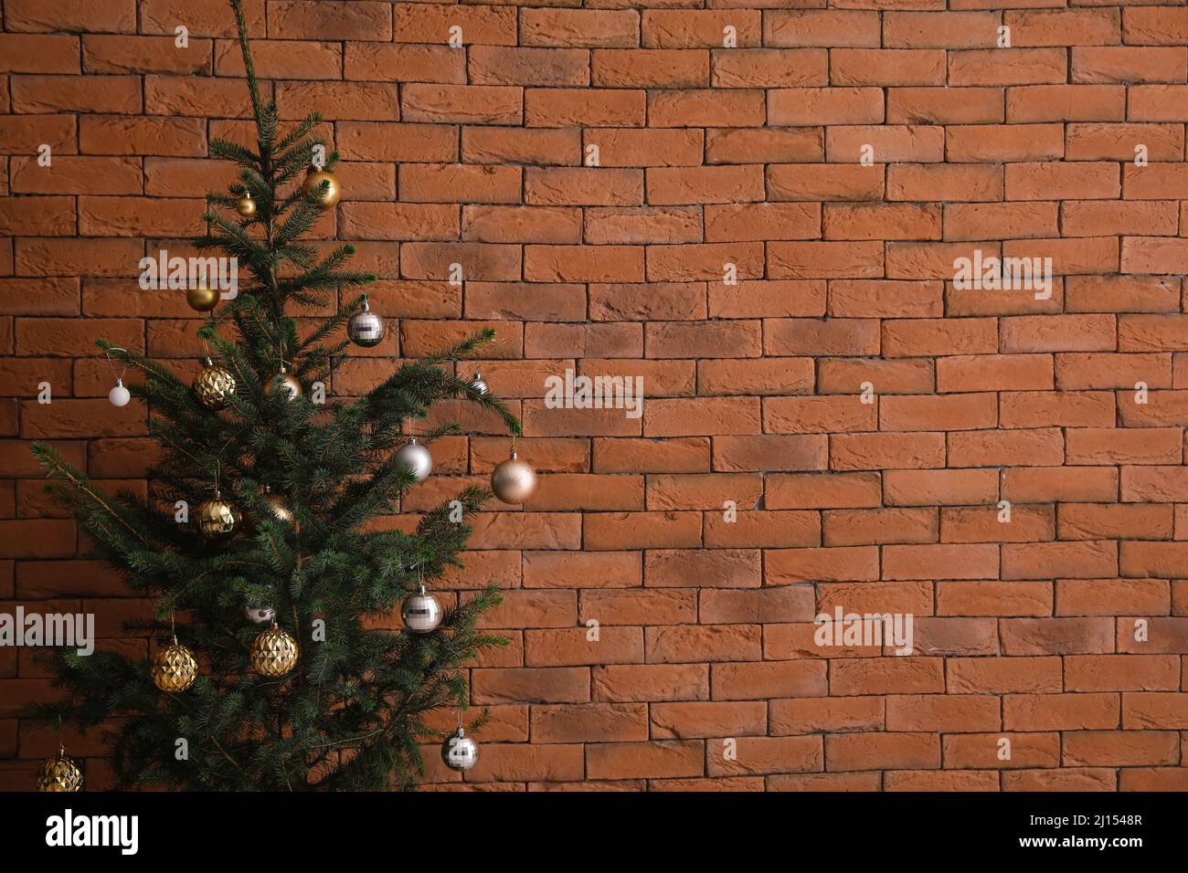 Beautiful decorated Christmas tree near brick wall in room Stock Photo ...