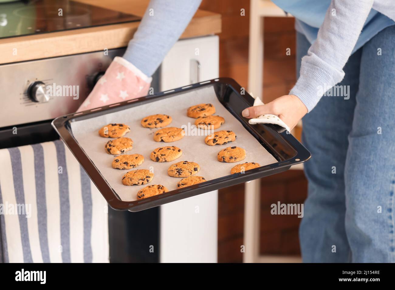 Mature woman holding baking dish with cookies near oven in kitchen ...