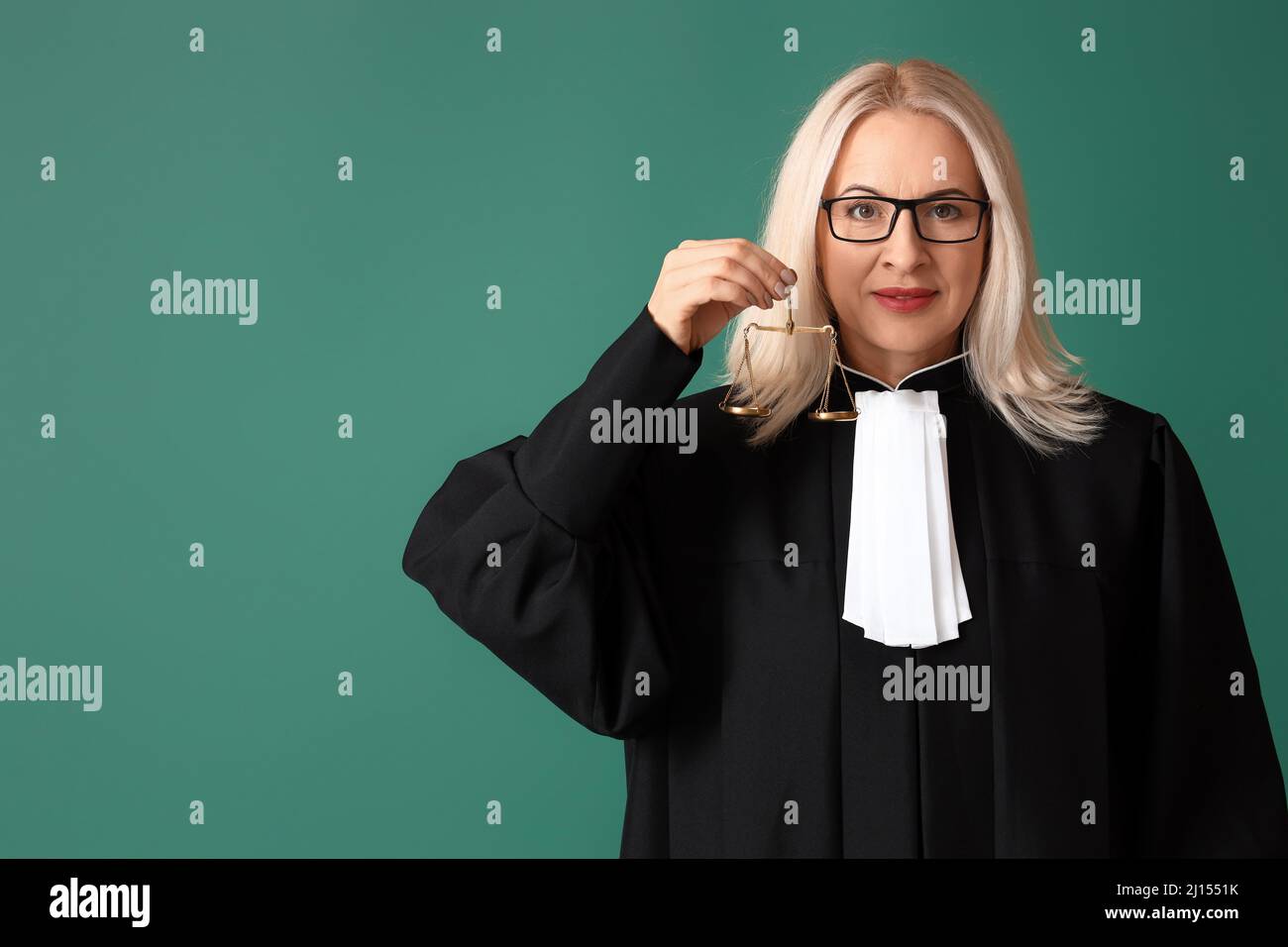 Mature female judge in robe with justice scales on green background ...