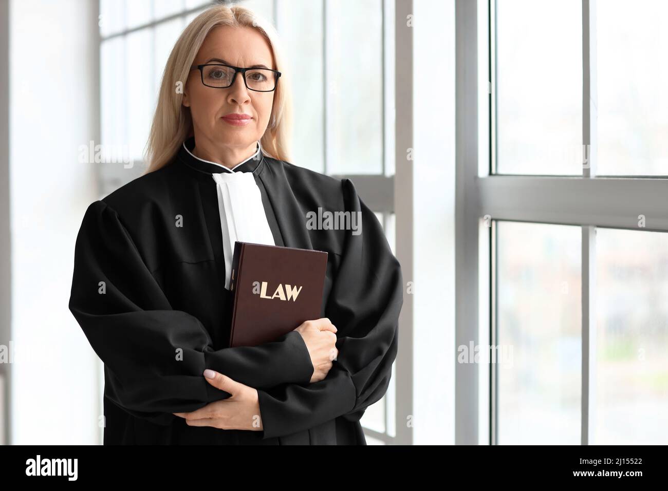 Mature female judge with law book near window in courtroom Stock Photo ...