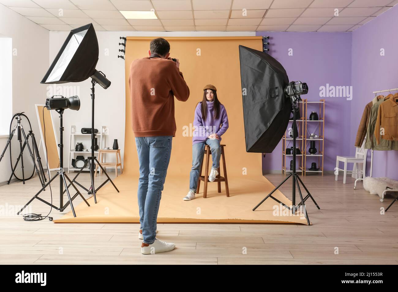 Male photographer taking picture of young woman sitting on stool in ...