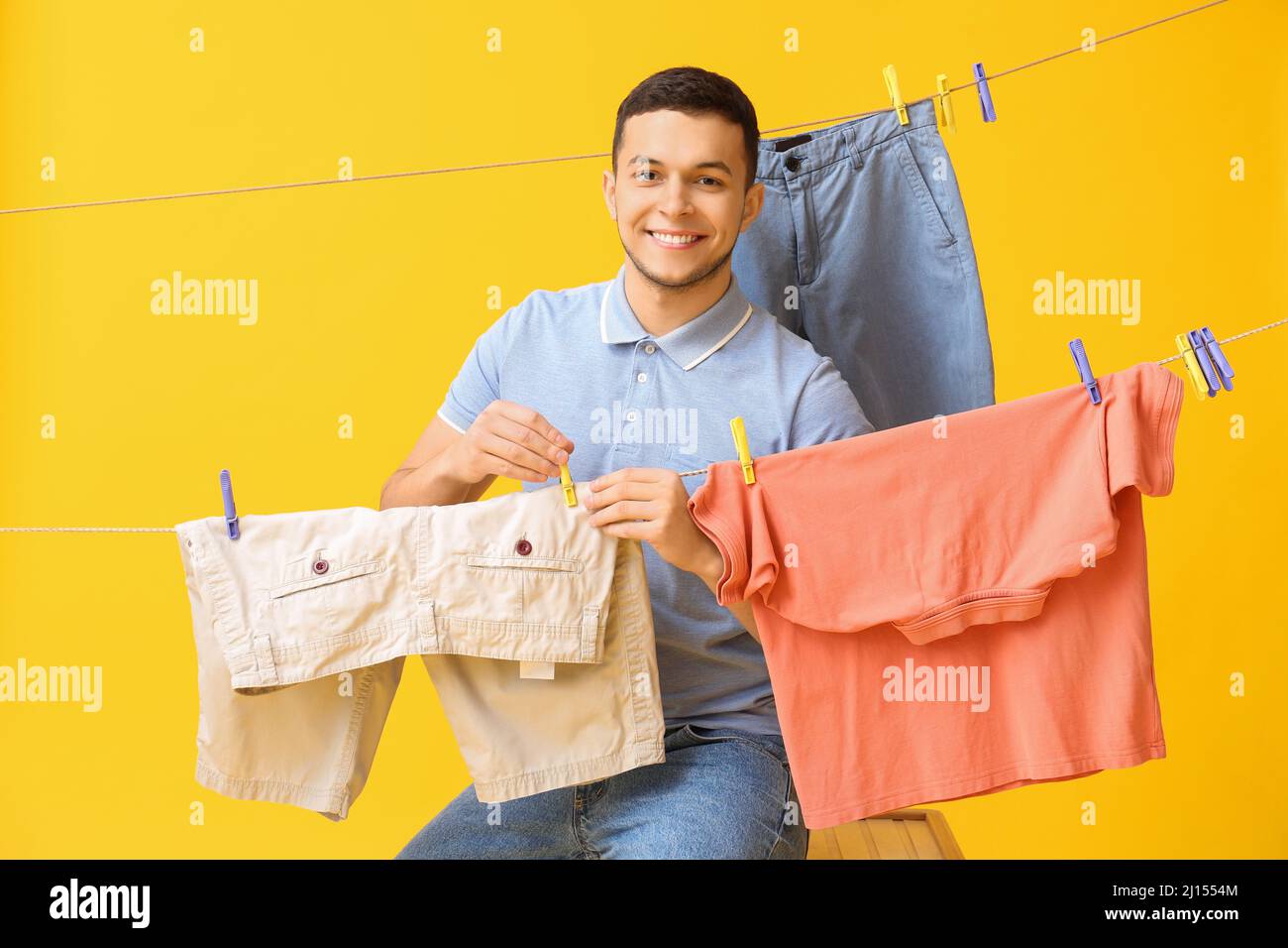 Young man hanging clean shorts with plastic clothespin on yellow ...