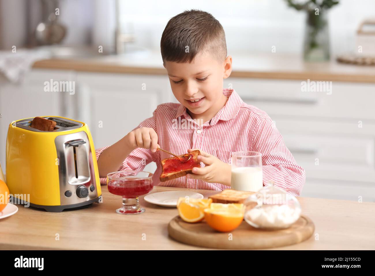 Cute little boy spreading jam onto toasted bread slice in kitchen Stock ...