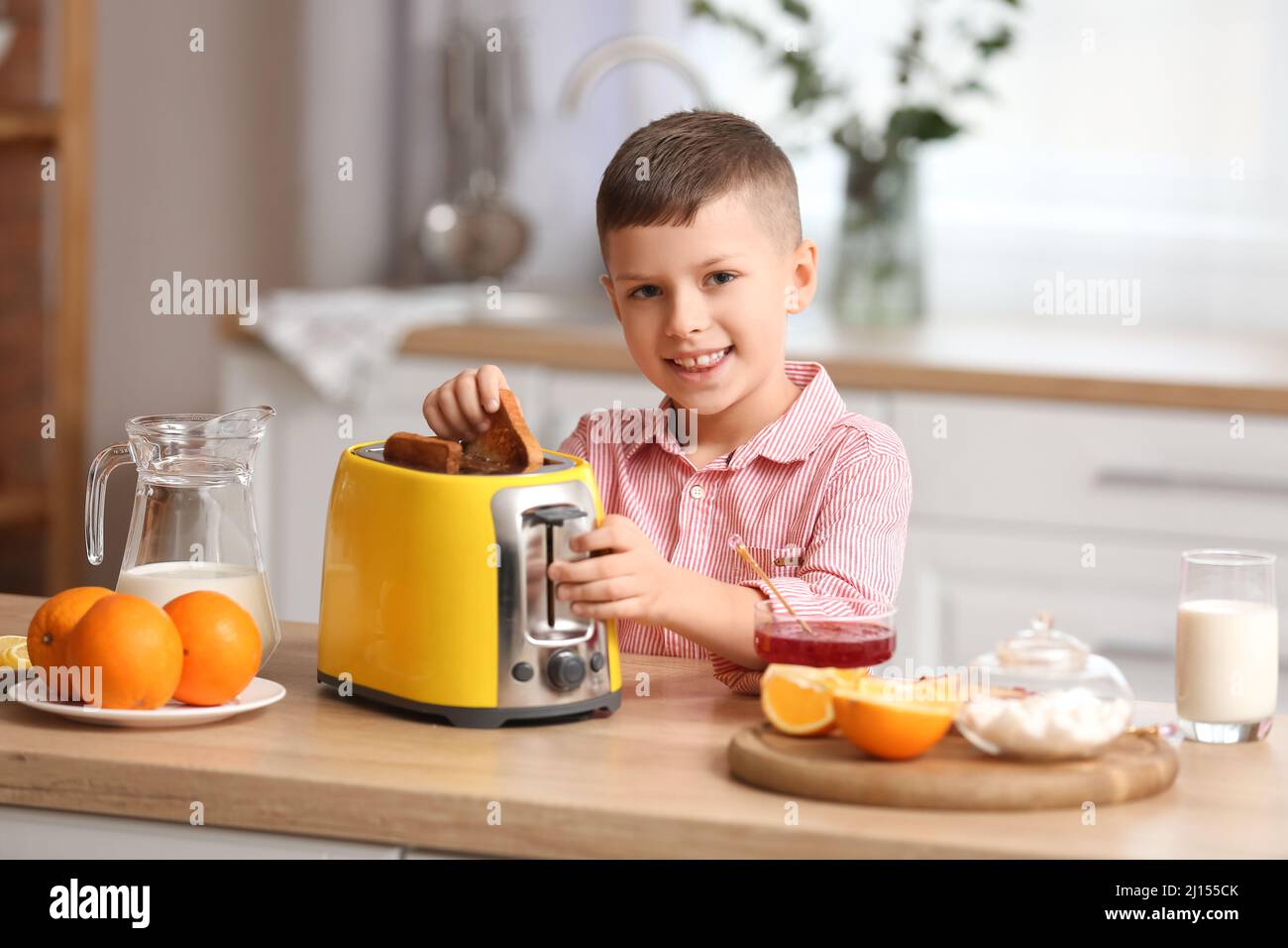 Cute little boy taking bread slice from yellow toaster in kitchen Stock ...